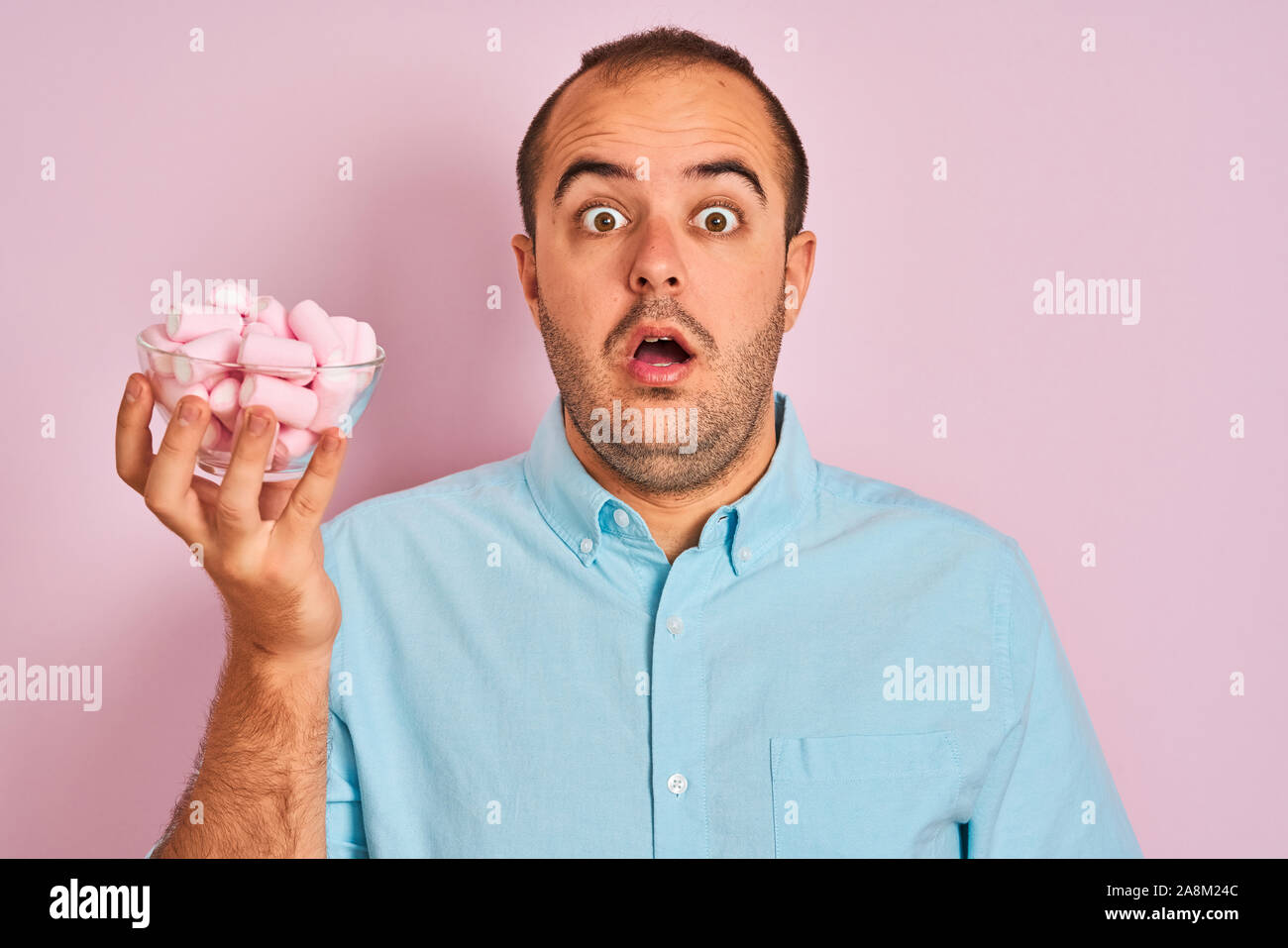 Young man holding bowl with marshmallows standing over isolated pink ...