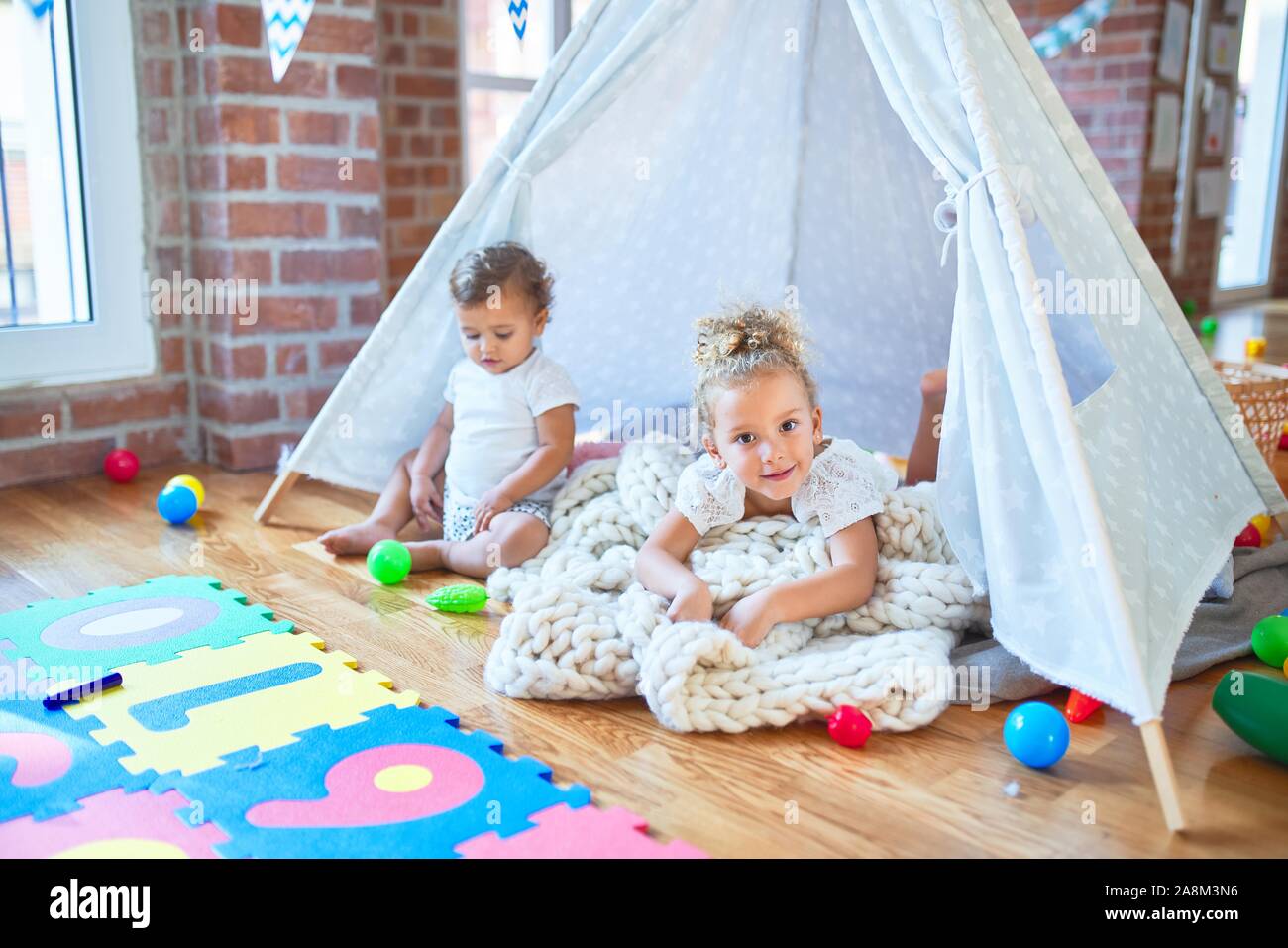 Beautiful toddlers playing inside tipi over blanket around lots of toys ...
