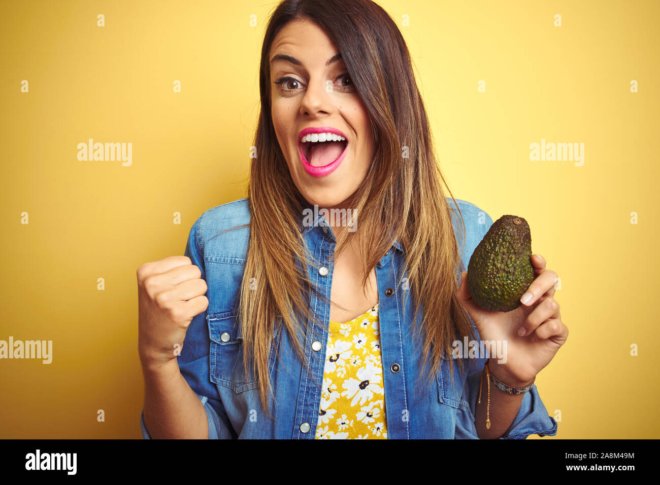 Young beautiful woman eating healthy avocado over yellow background ...