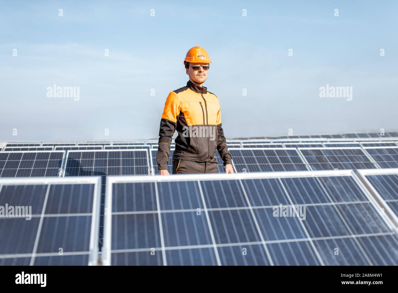 Well-equipped worker in protective orange clothing servicing solar ...