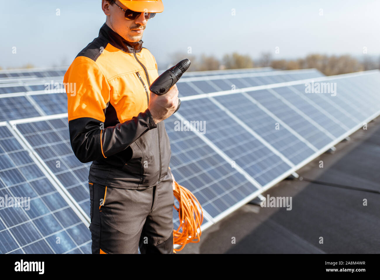 Well-equipped worker in protective orange clothing servicing solar ...