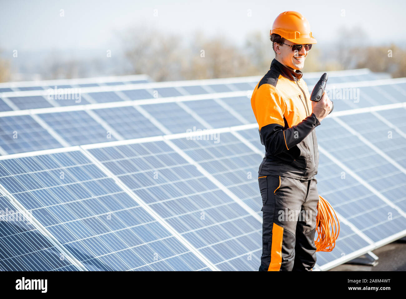 Well-equipped worker in protective orange clothing servicing solar ...