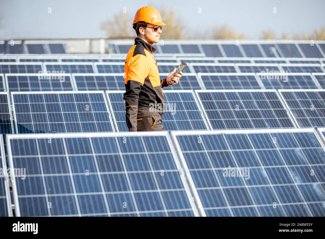 Well-equipped worker in protective orange clothing servicing solar ...