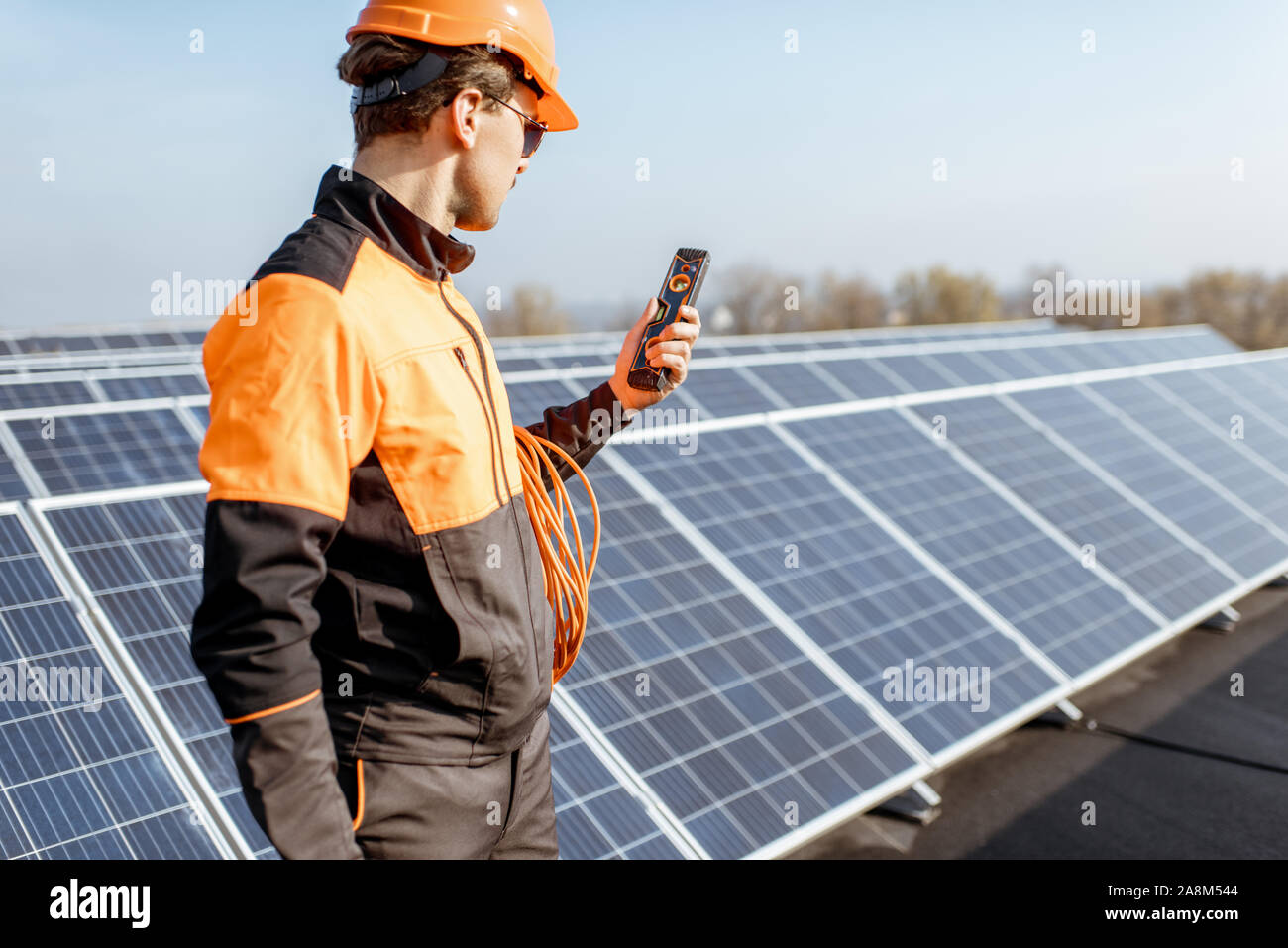 Well-equipped worker in protective orange clothing servicing solar ...