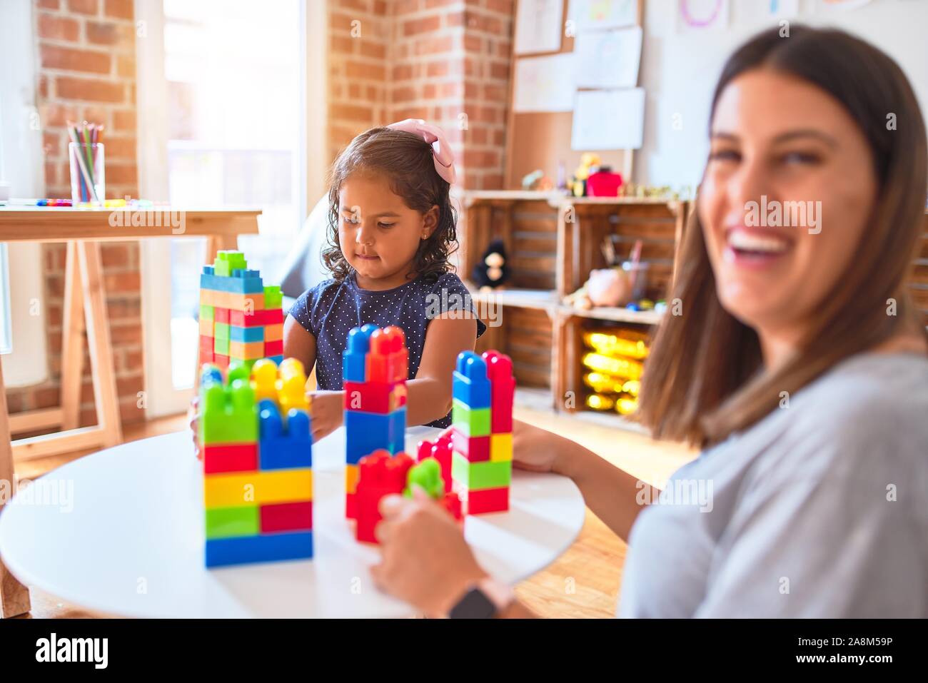 Beautiful teacher and toddler girl playing with construction blocks ...