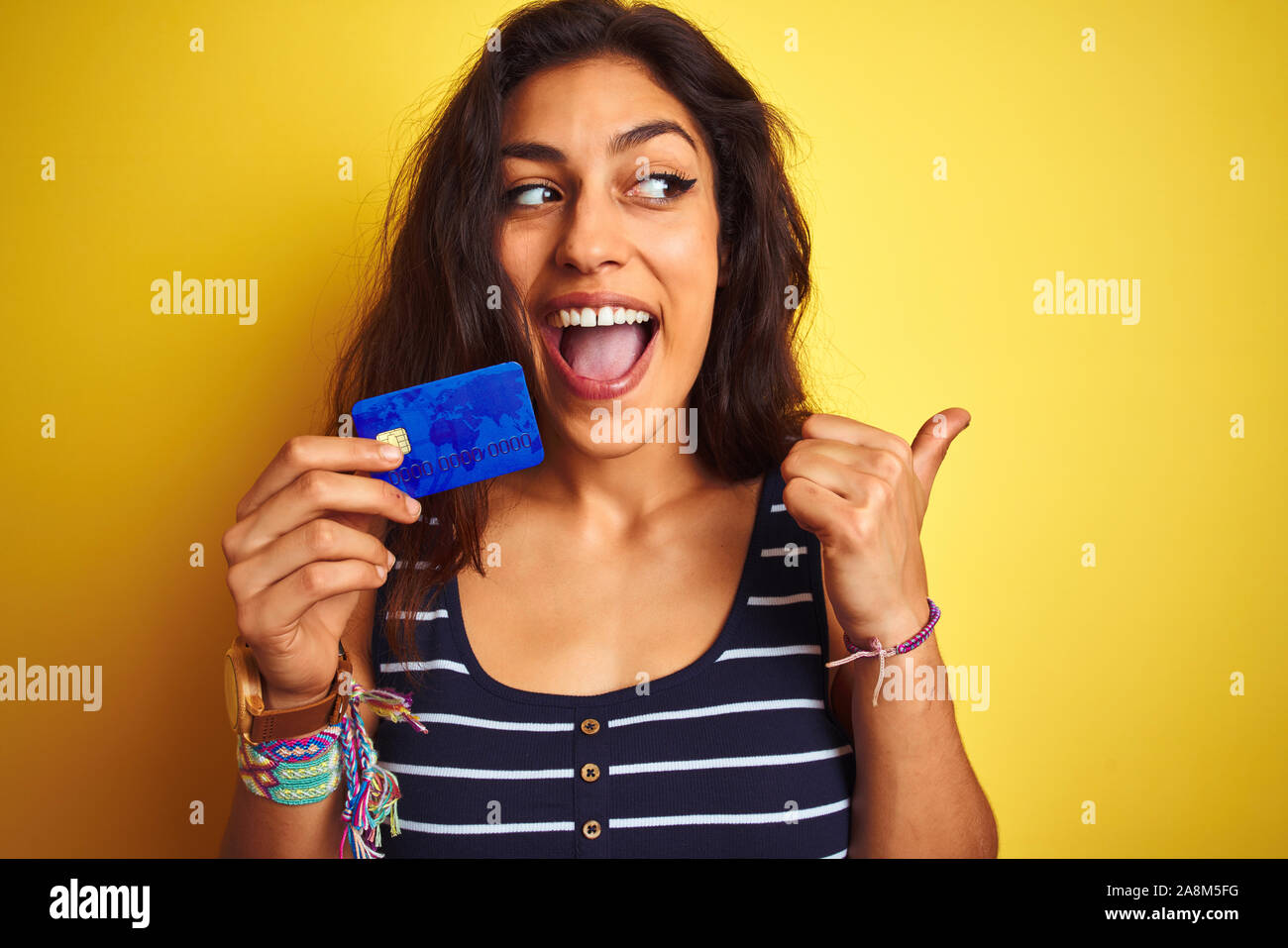 Young beautiful woman holding credit card standing over isolated yellow ...