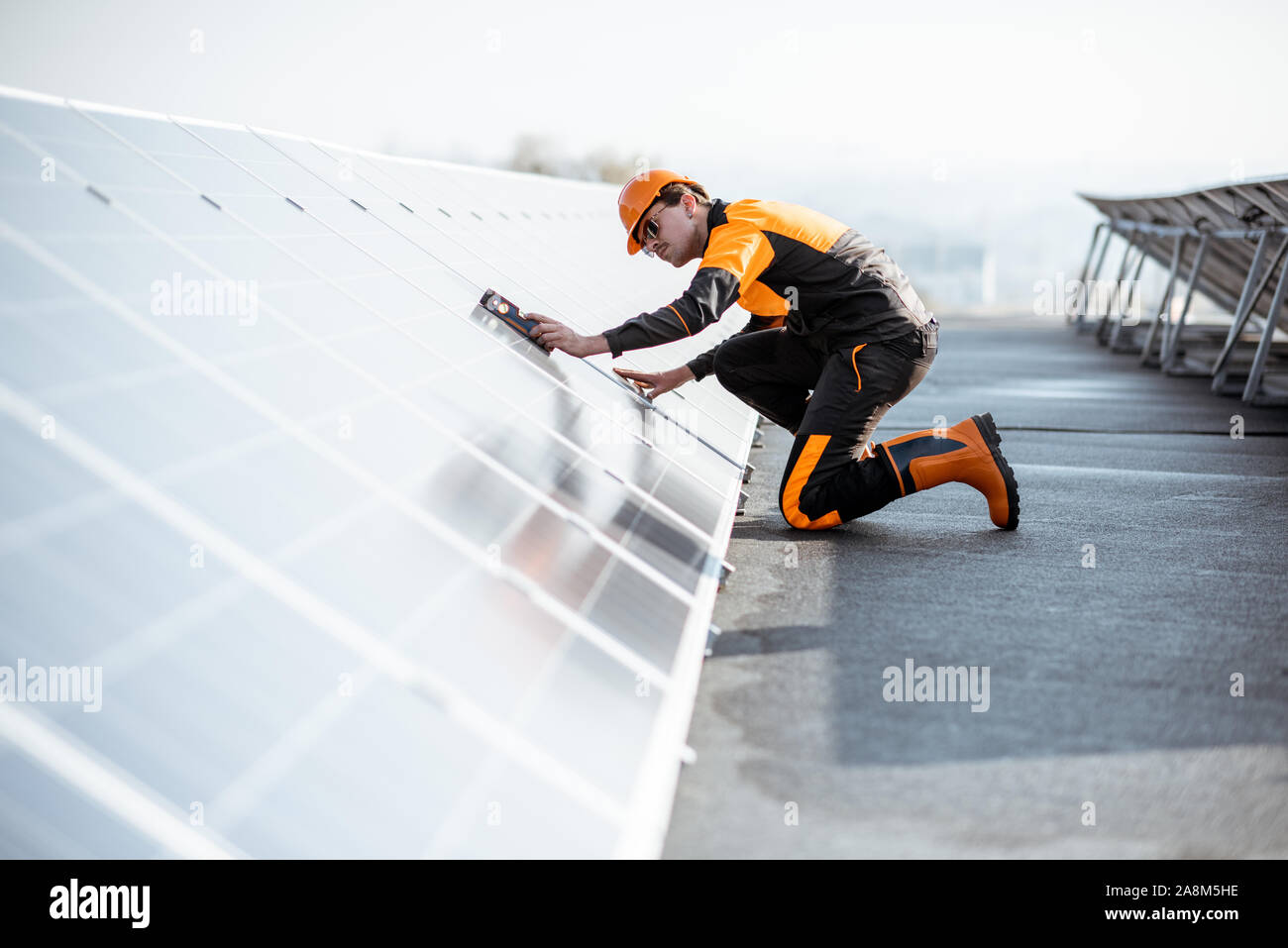 Well-equipped worker in protective orange clothing installing solar ...