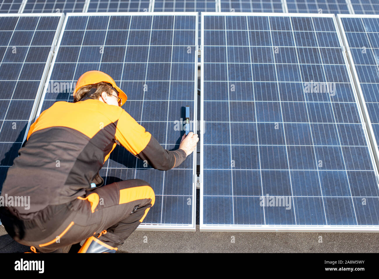 Well-equipped worker in protective orange clothing installing solar ...