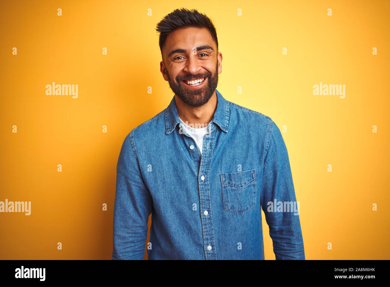 Young indian man wearing denim shirt standing over isolated yellow ...