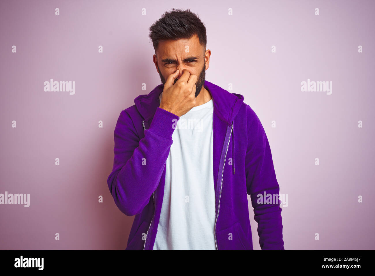 Young indian man wearing purple sweatshirt standing over isolated pink ...