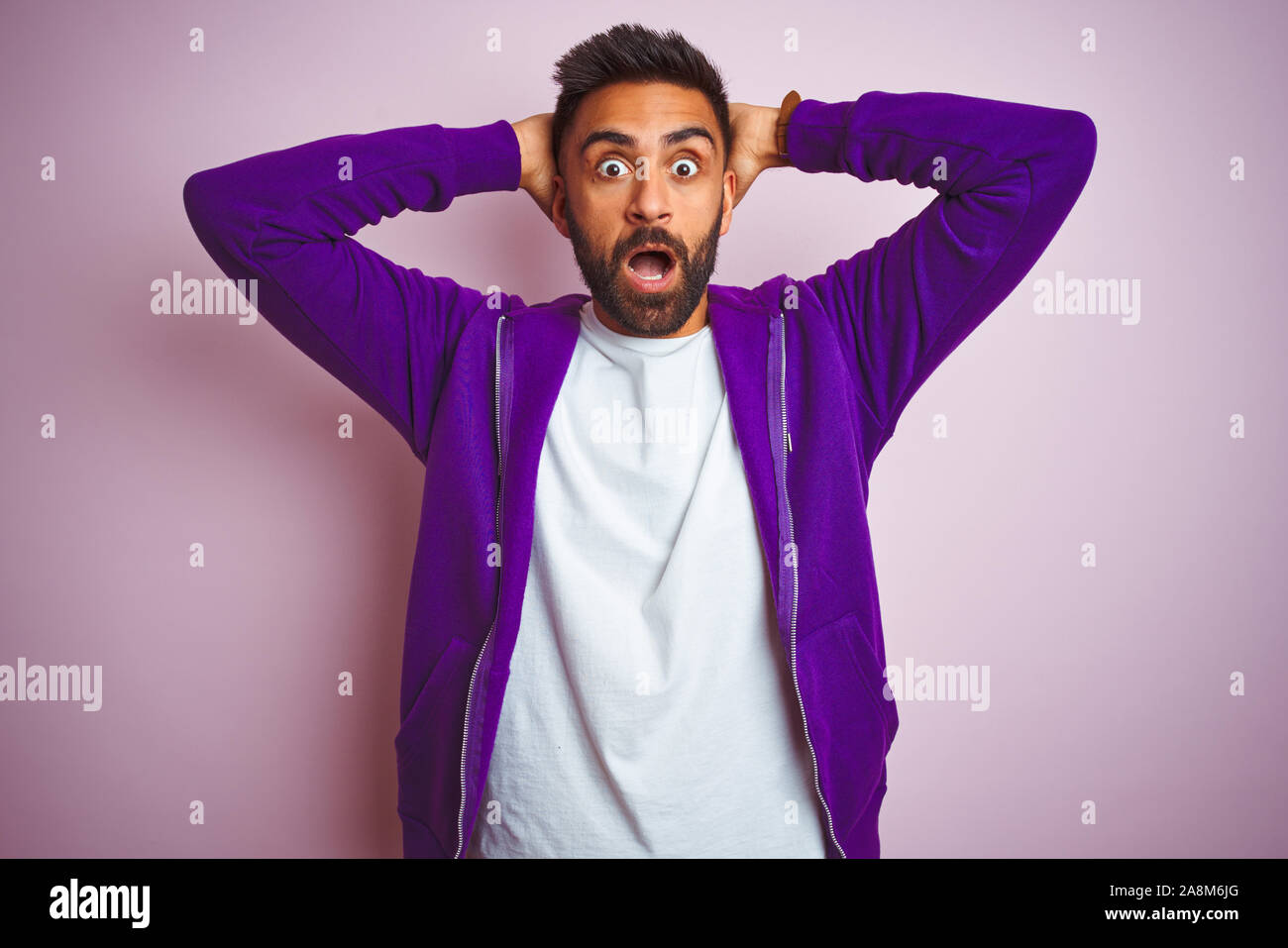 Young indian man wearing purple sweatshirt standing over isolated pink ...