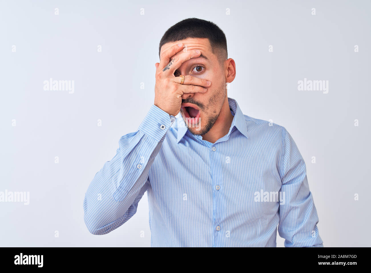 Young handsome business man standing over isolated background peeking in shock covering face and ...