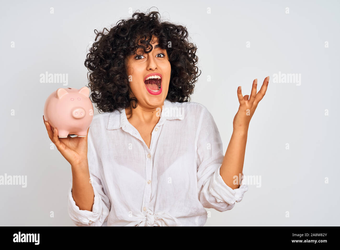 Young arab woman with curly hair holding piggy bank over isolated white ...