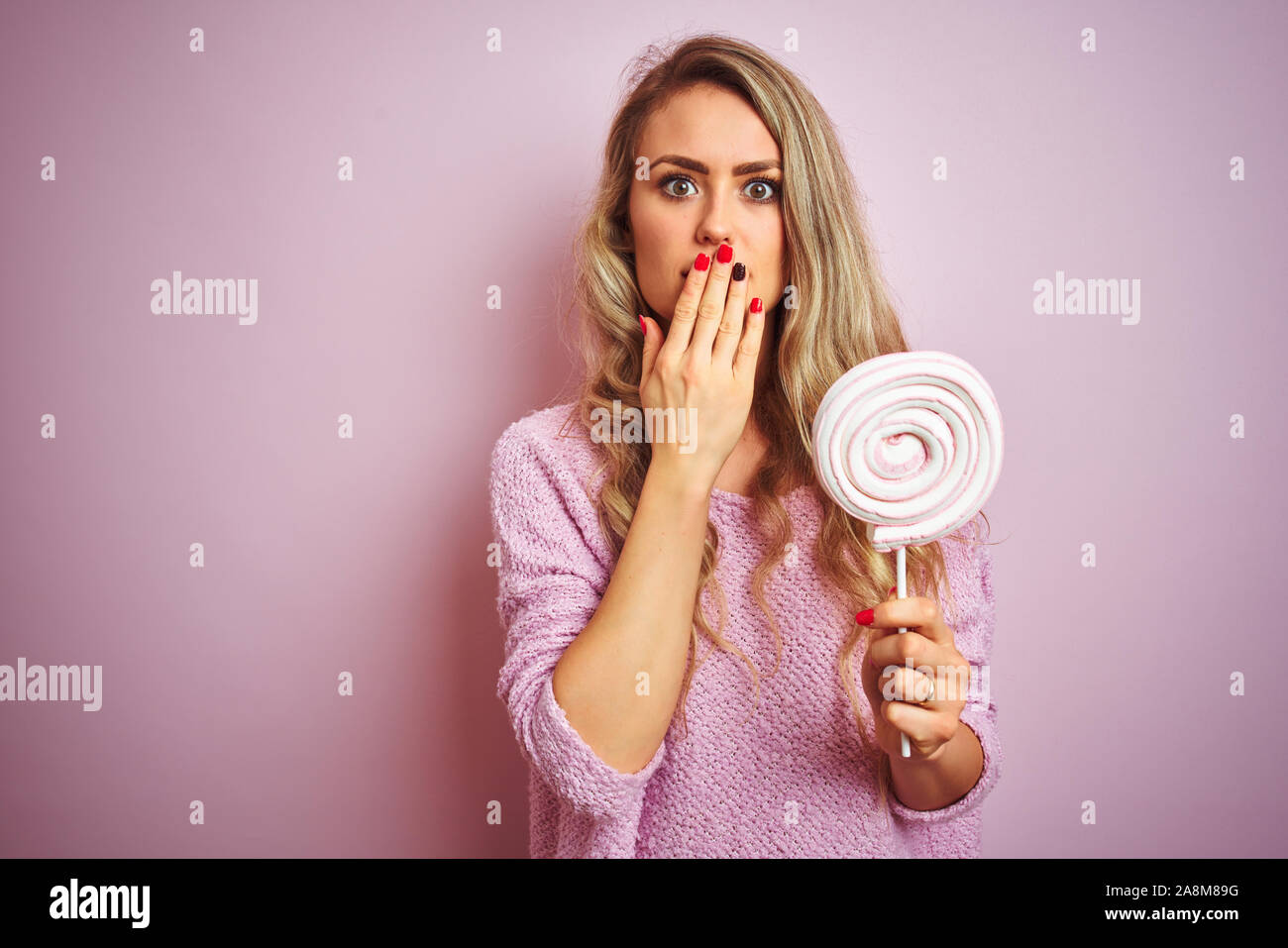 Young beautiful woman eating sweet candy over pink isolated background ...