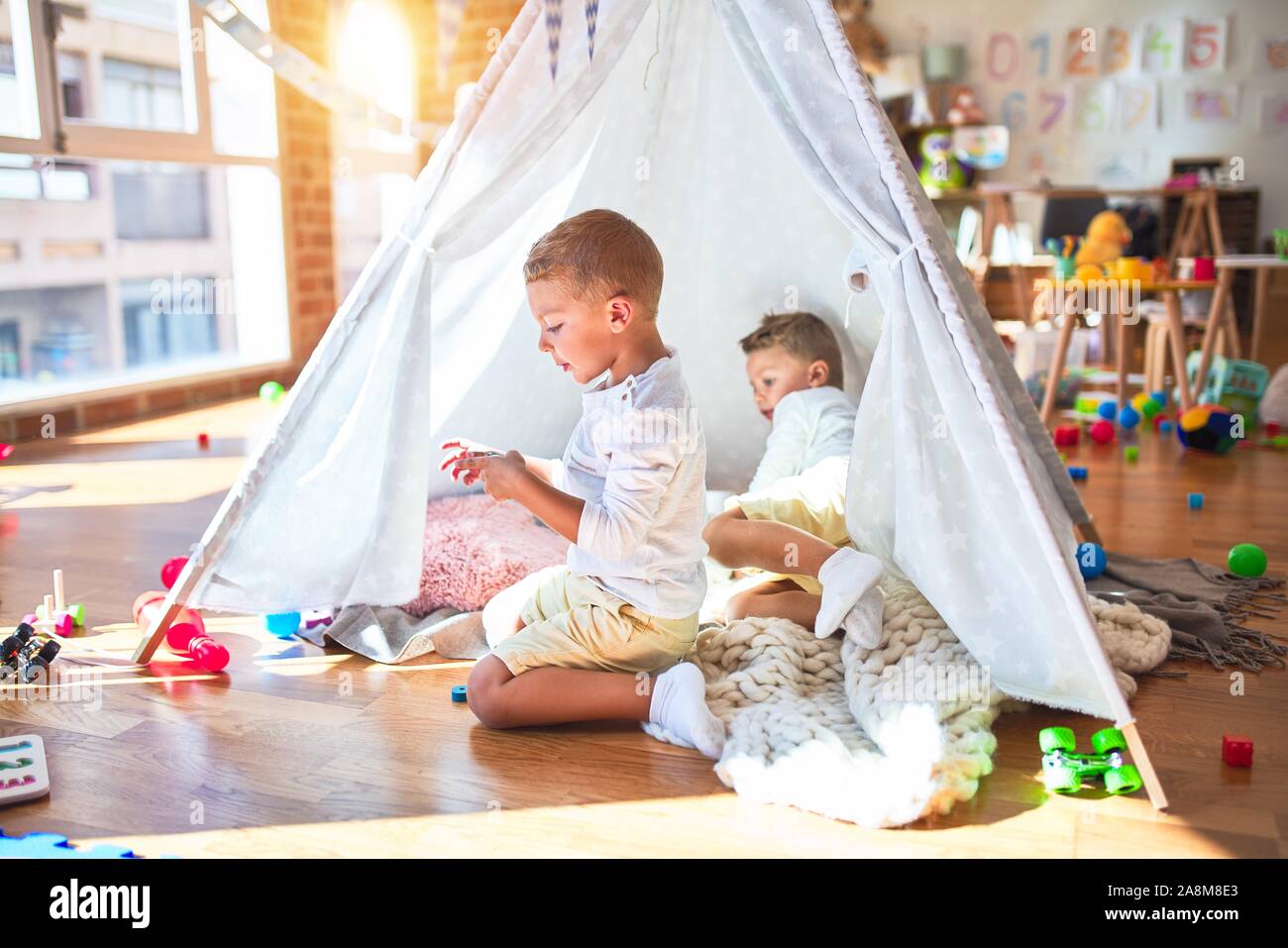 Adorable blonde twins playing inside tipi around lots of toys at ...