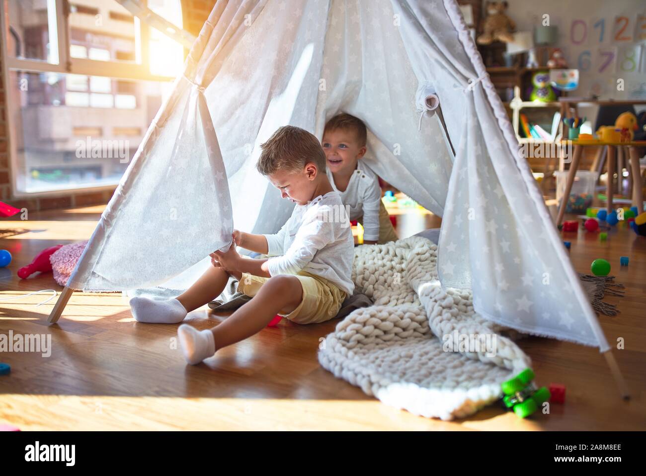 Adorable blonde twins playing inside tipi around lots of toys at ...