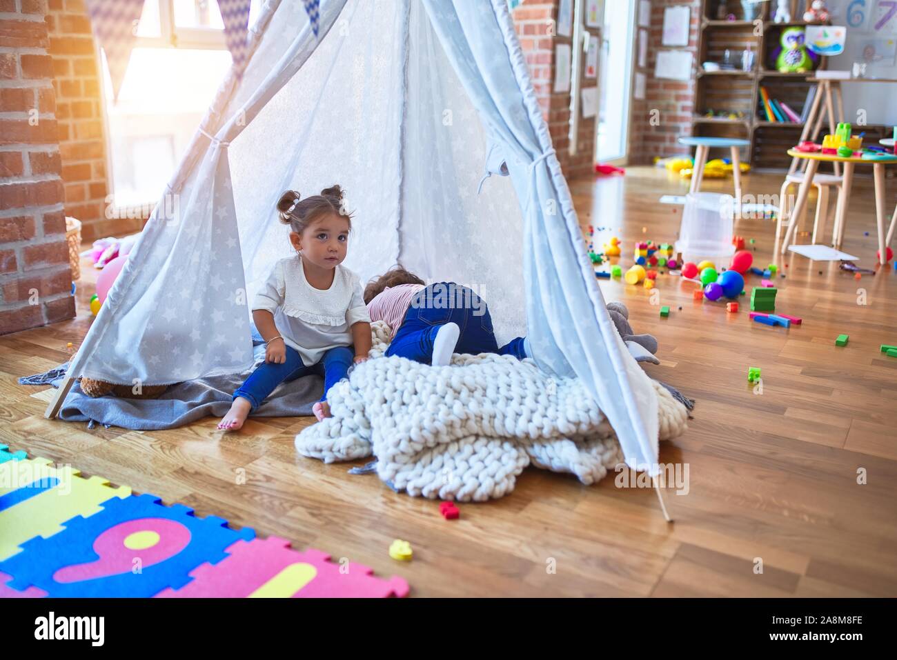 Adorable toddlers lying down over blanket inside tipi smiling at ...