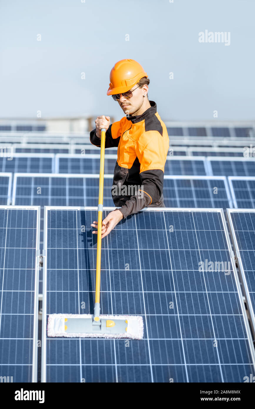Professional cleaner in protective workwear cleaning solar panels with ...