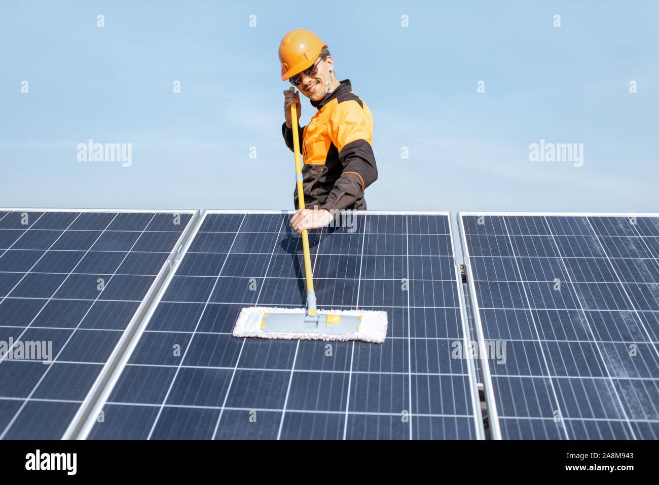 Professional cleaner in protective workwear cleaning solar panels with ...