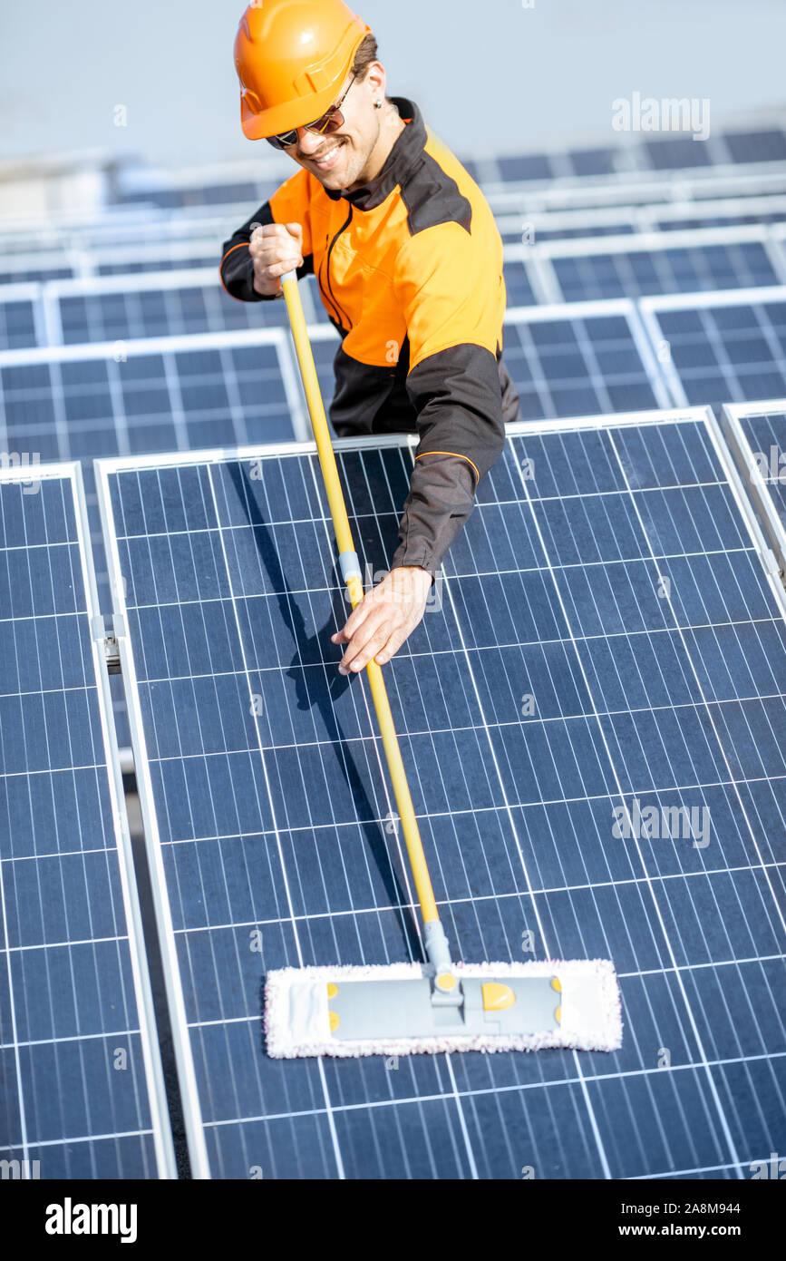 Professional cleaner in protective workwear cleaning solar panels with ...