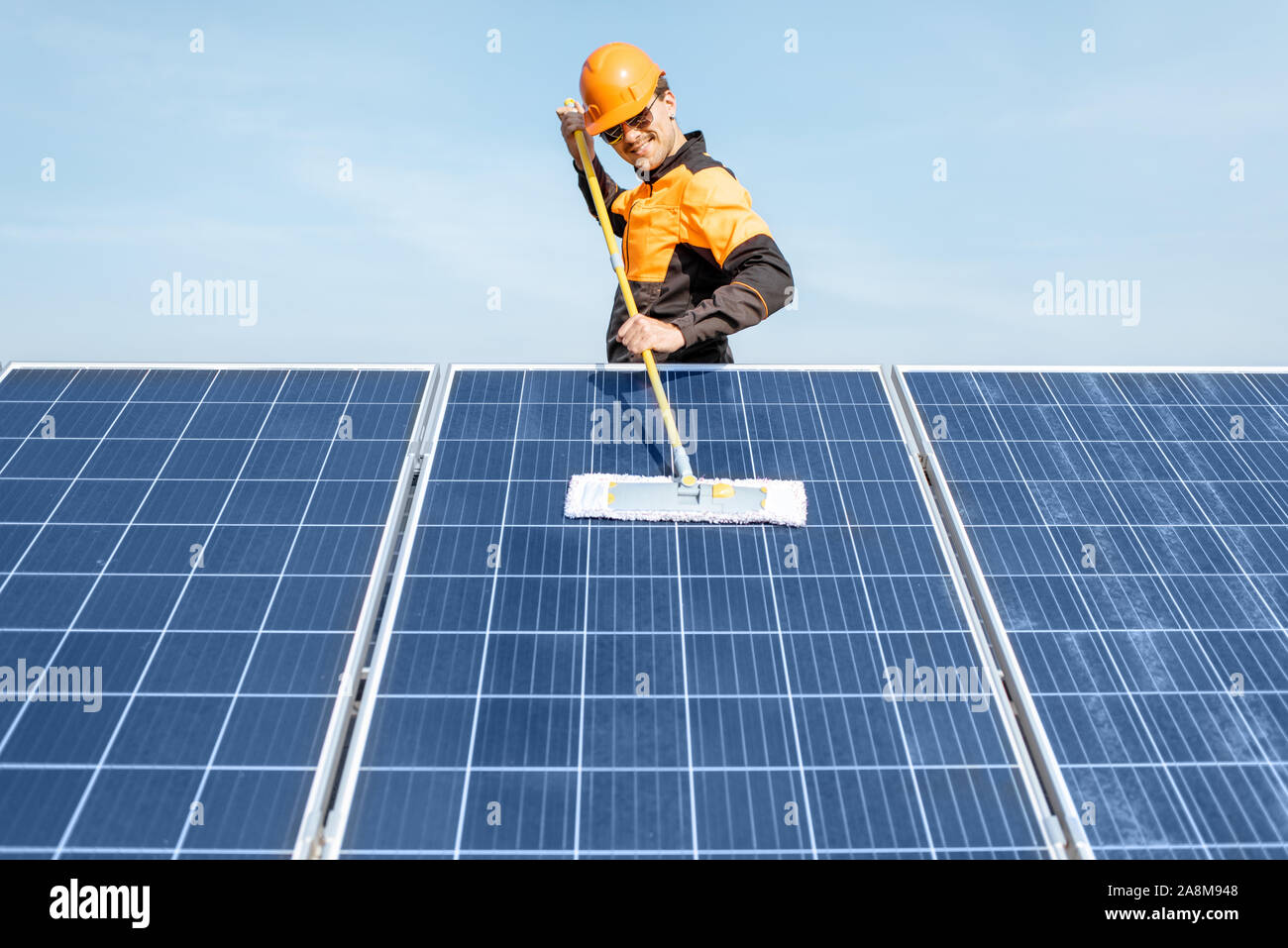 Professional cleaner in protective workwear cleaning solar panels with ...