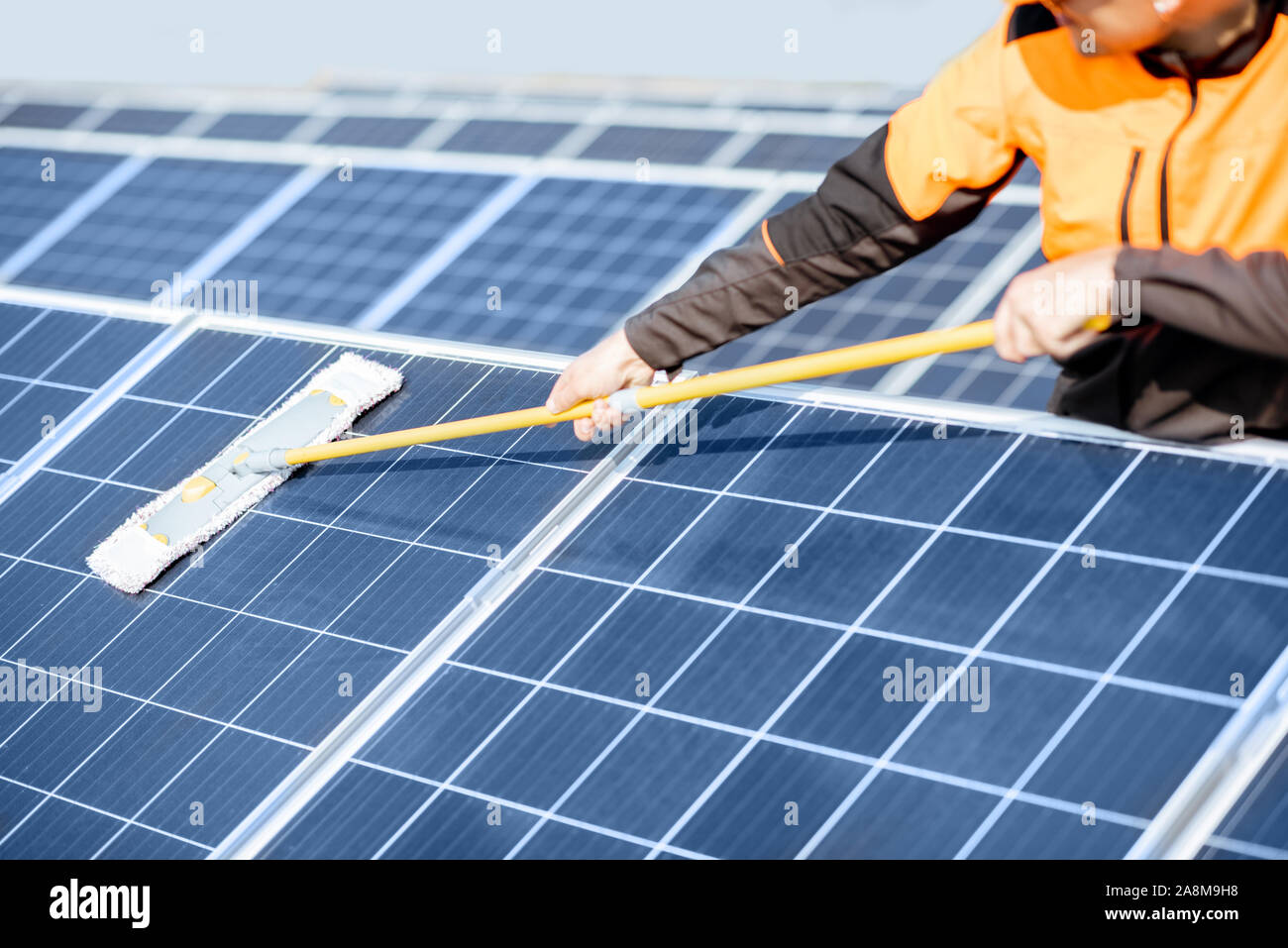 Professional cleaner in protective workwear cleaning solar panels with ...