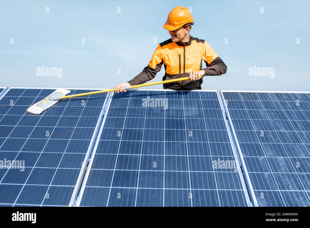 Professional cleaner in protective workwear cleaning solar panels with ...