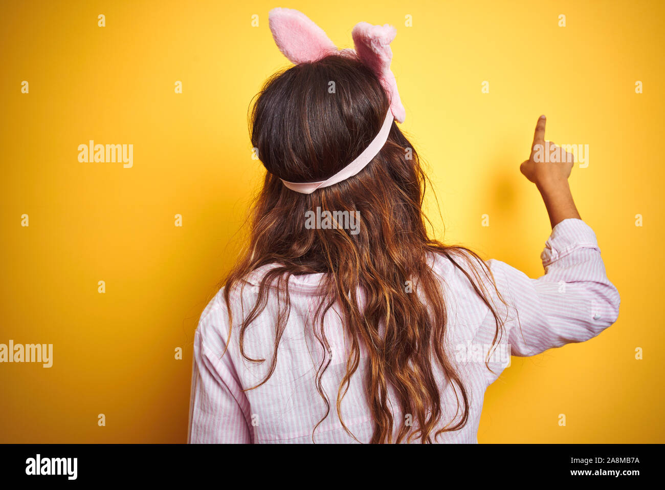 Young woman wearing pajama and sleep mask standing over yellow isolated ...
