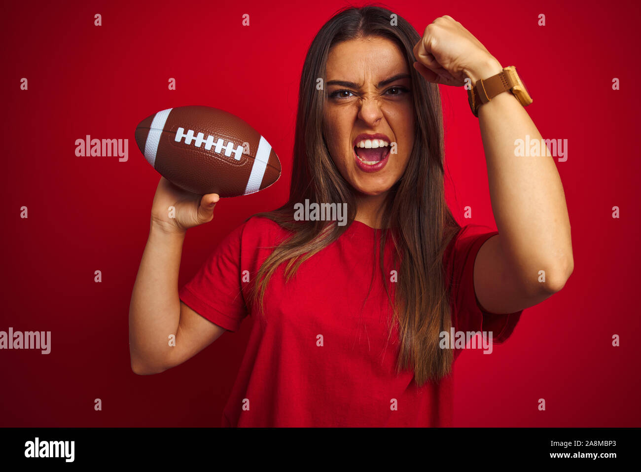 Young beautiful sportswoman holding football ball over isolated red ...
