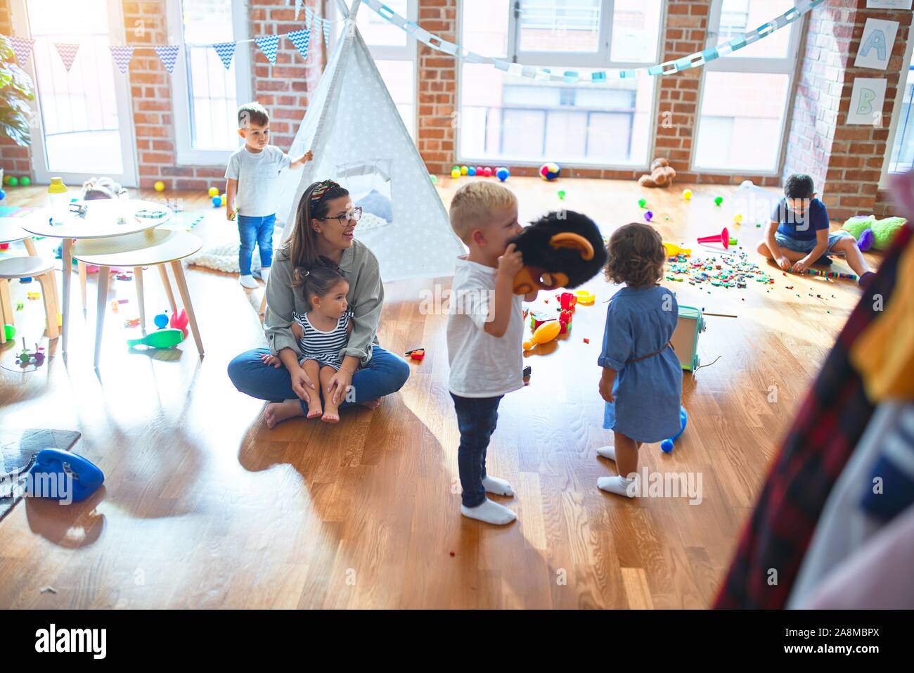 Beautiful teacher and group of toddlers playing around lots of toys at ...