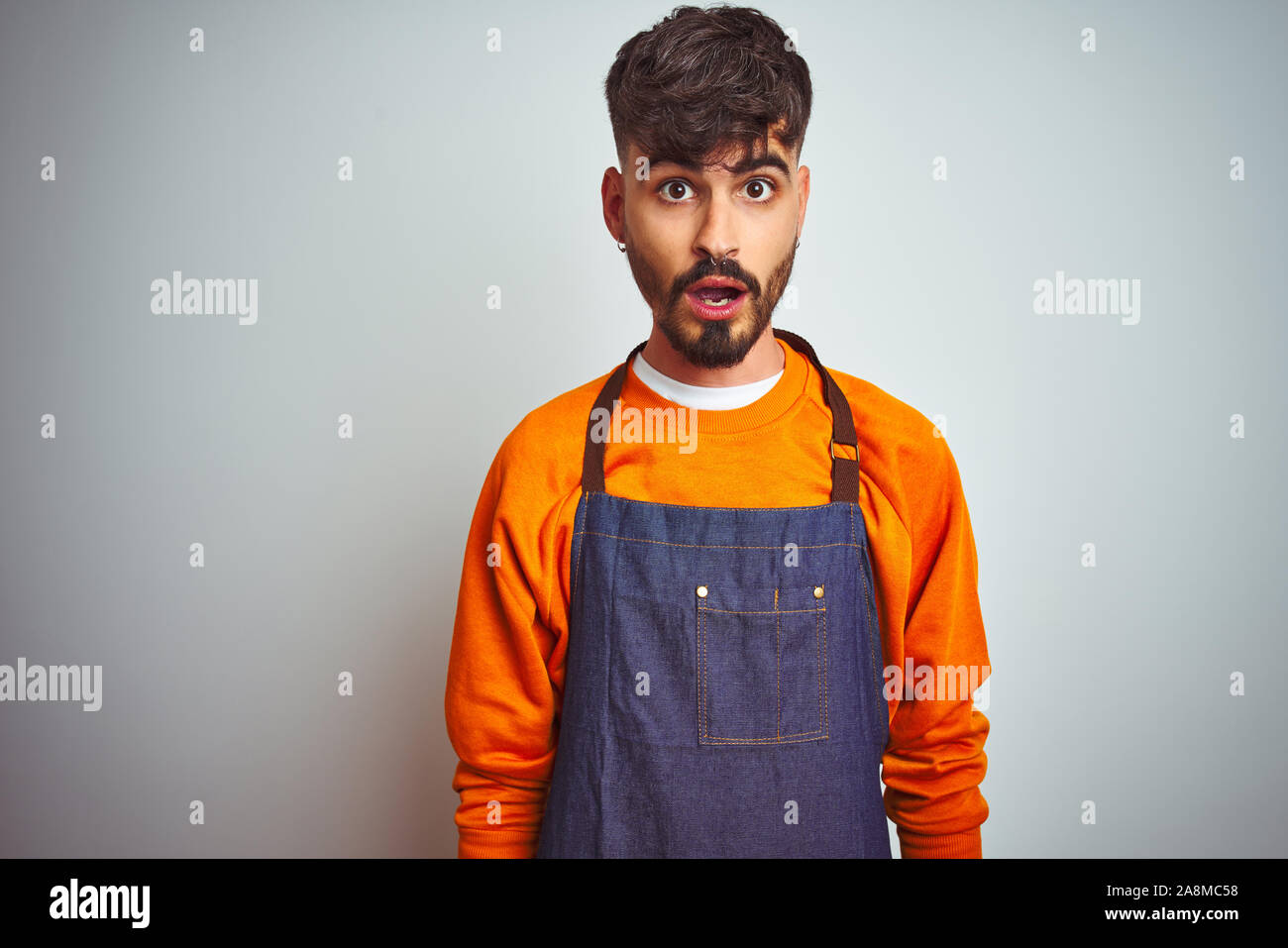 Young shopkeeper man with tattoo wearing apron standing over isolated ...