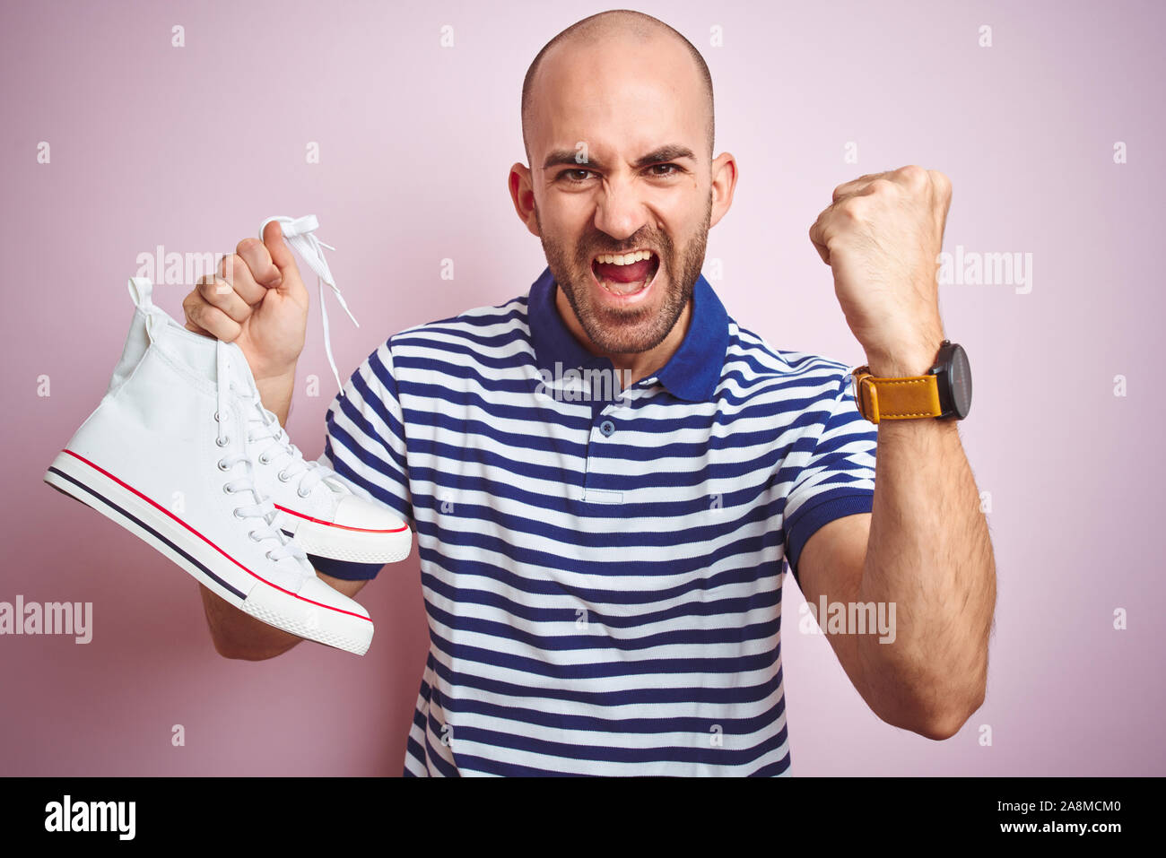 Young man holding casual sneakers shoes over pink isolated background ...