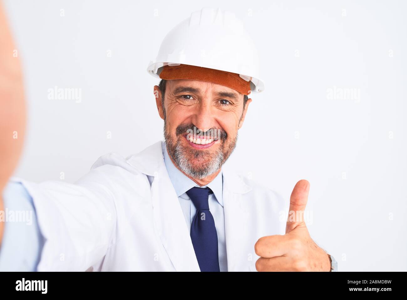 Middle age engineer man wearing helmet make selfie over isolated white ...