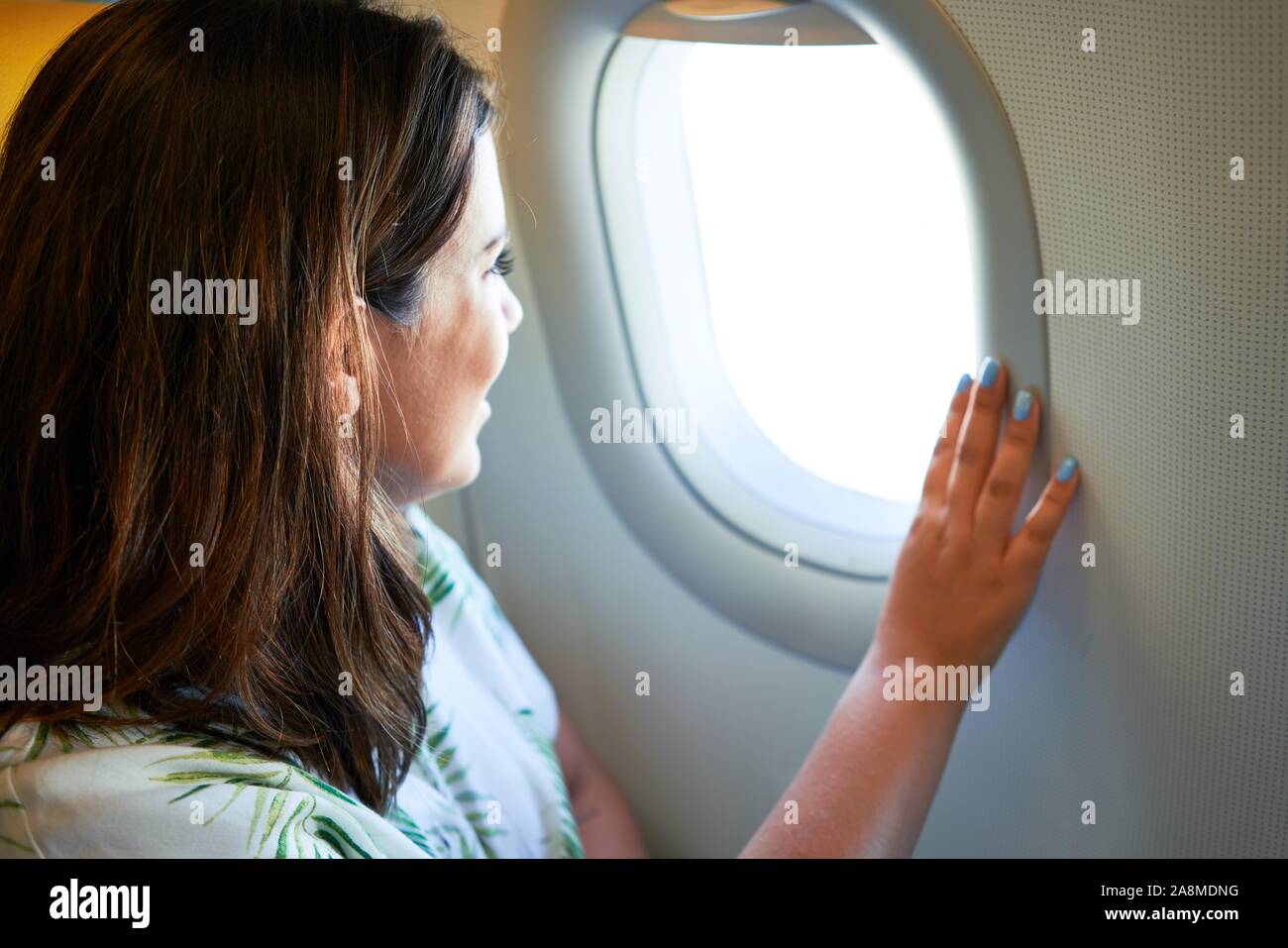 Young traveller woman sitting inside plane at the airport with sky view ...