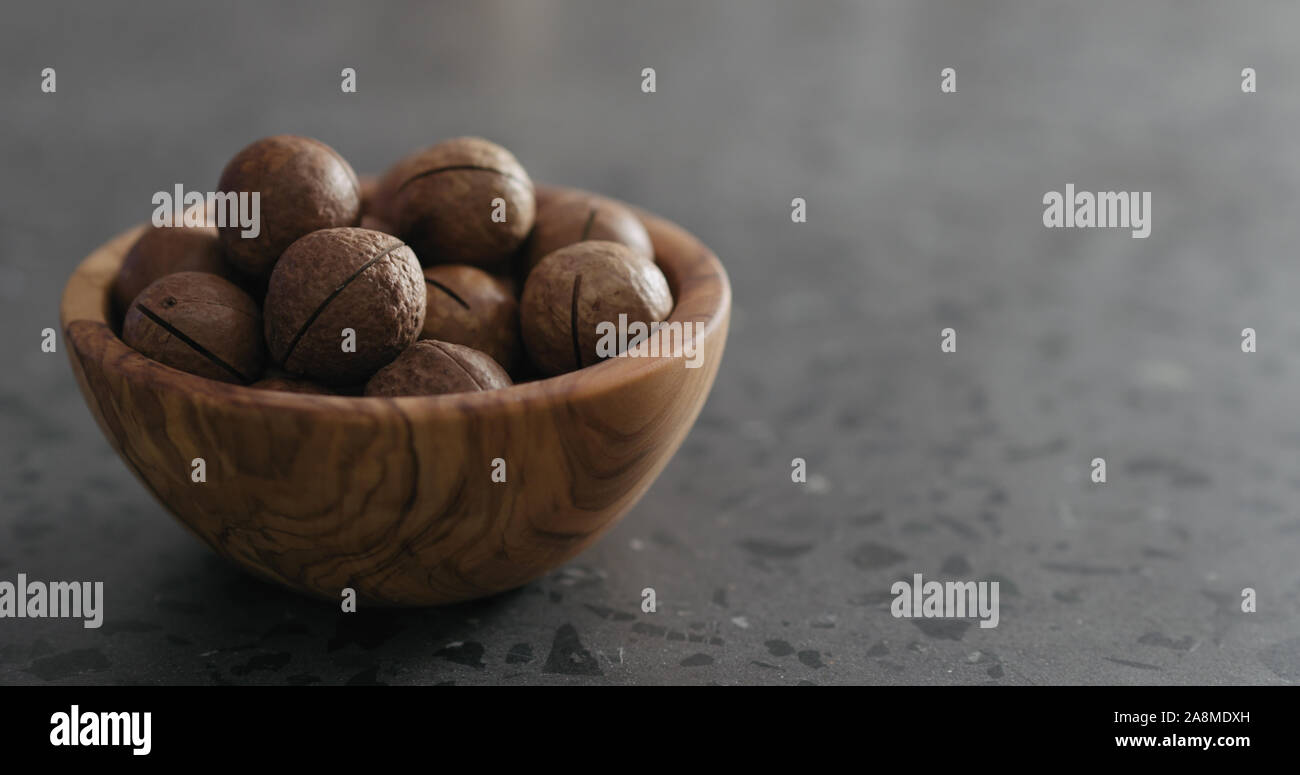 inshell macadamia nuts in olive wood bowl on terrazzo surface, wide ...