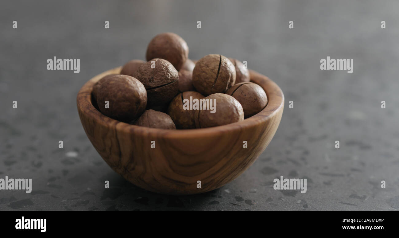 inshell macadamia nuts in olive wood bowl on terrazzo surface, wide ...