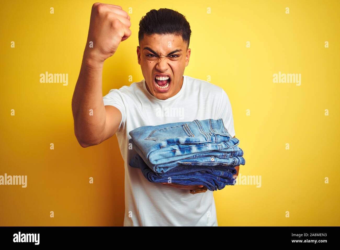 Young brazilian shopkeeper man holding jeans standing over isolated ...