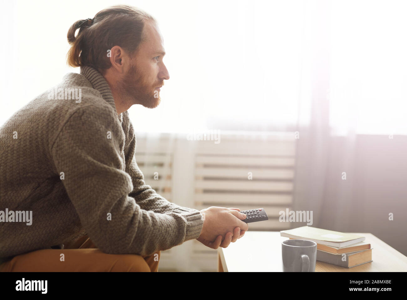 Side view portrait of modern bearded man watching TV at home and ...
