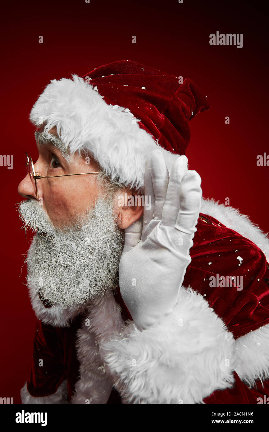 Portrait of classic Santa Claus putting hand to ear trying to hear ...