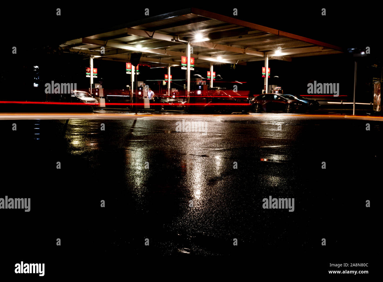 Gas station at night with lights from passing cars as people fill up ...