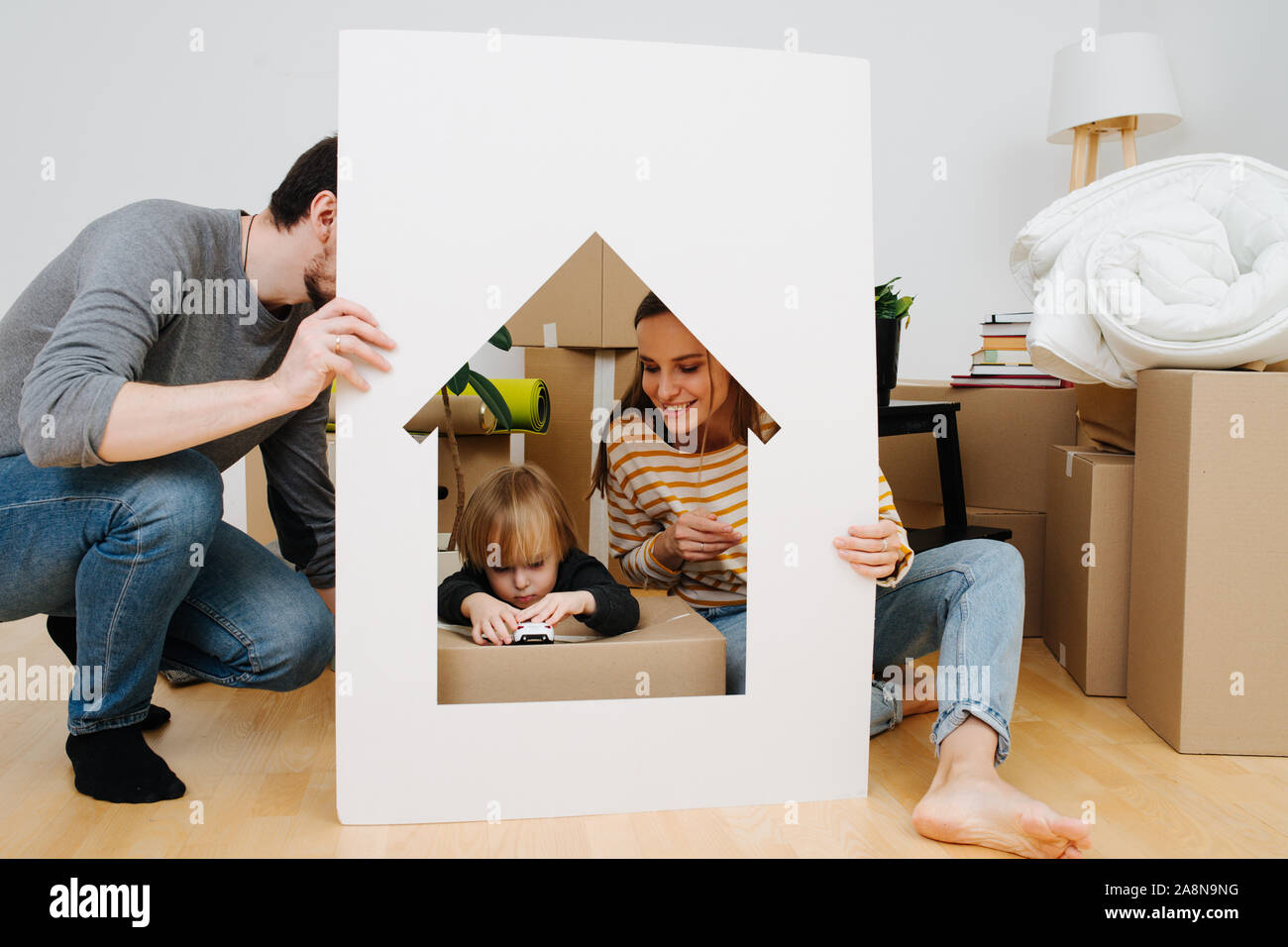 Little boy playing inside a house resembling frame, held by his parents ...