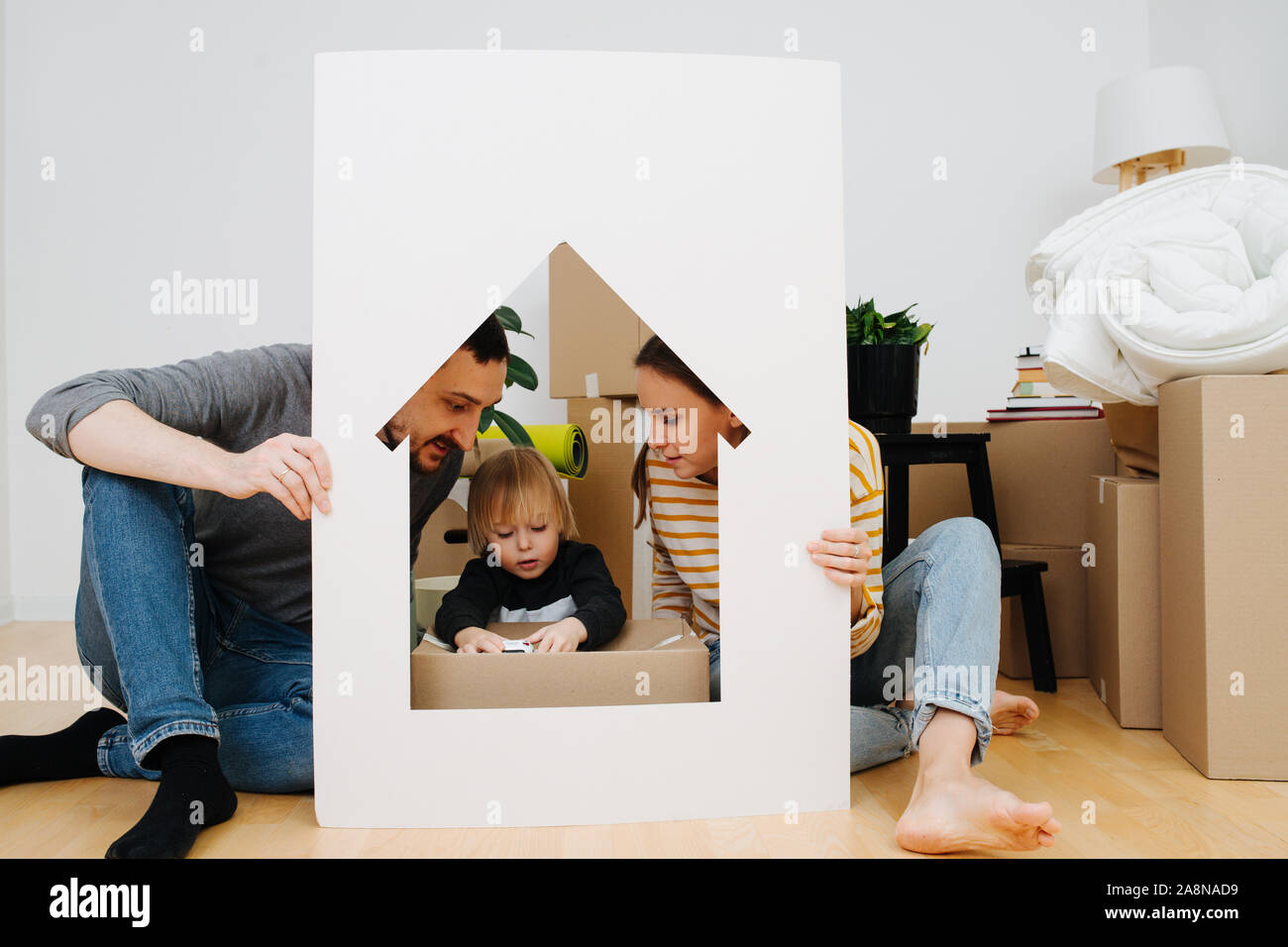 Little boy playing inside a house resembling frame, held by his parents ...