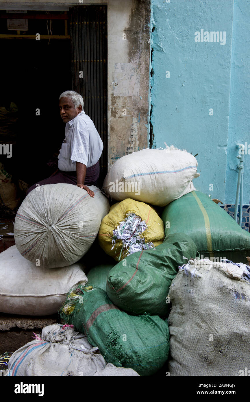 A man sitting on top of bags of paper to be recycled. Yangon Myanmar ...