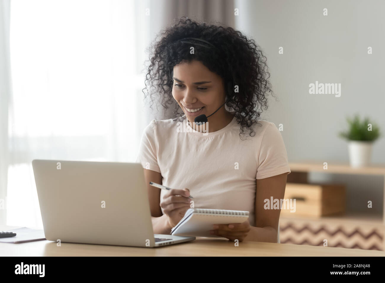 Smiling African American woman in headset writing notes in notepad ...