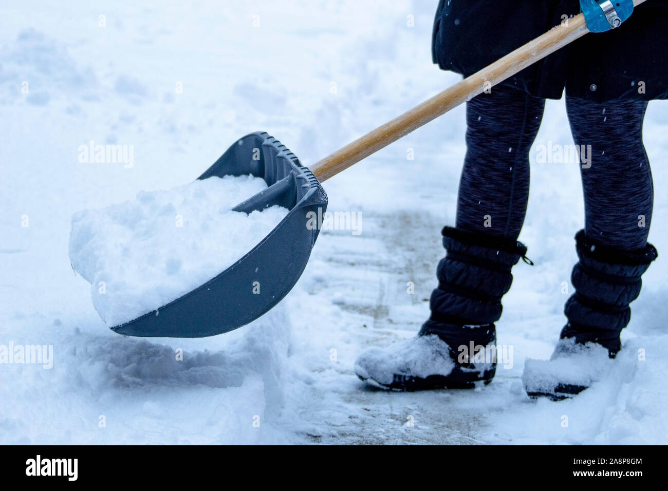 Female shovelling snow with a full snow shovel on a side view, during ...