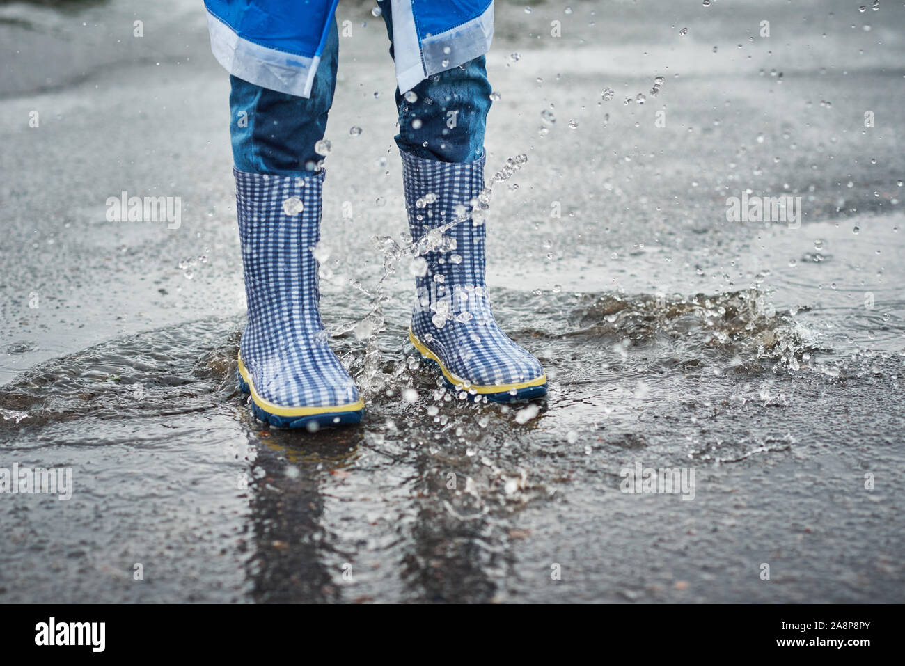 child in blue rubber boots jumping over puddle in the rain Stock Photo ...