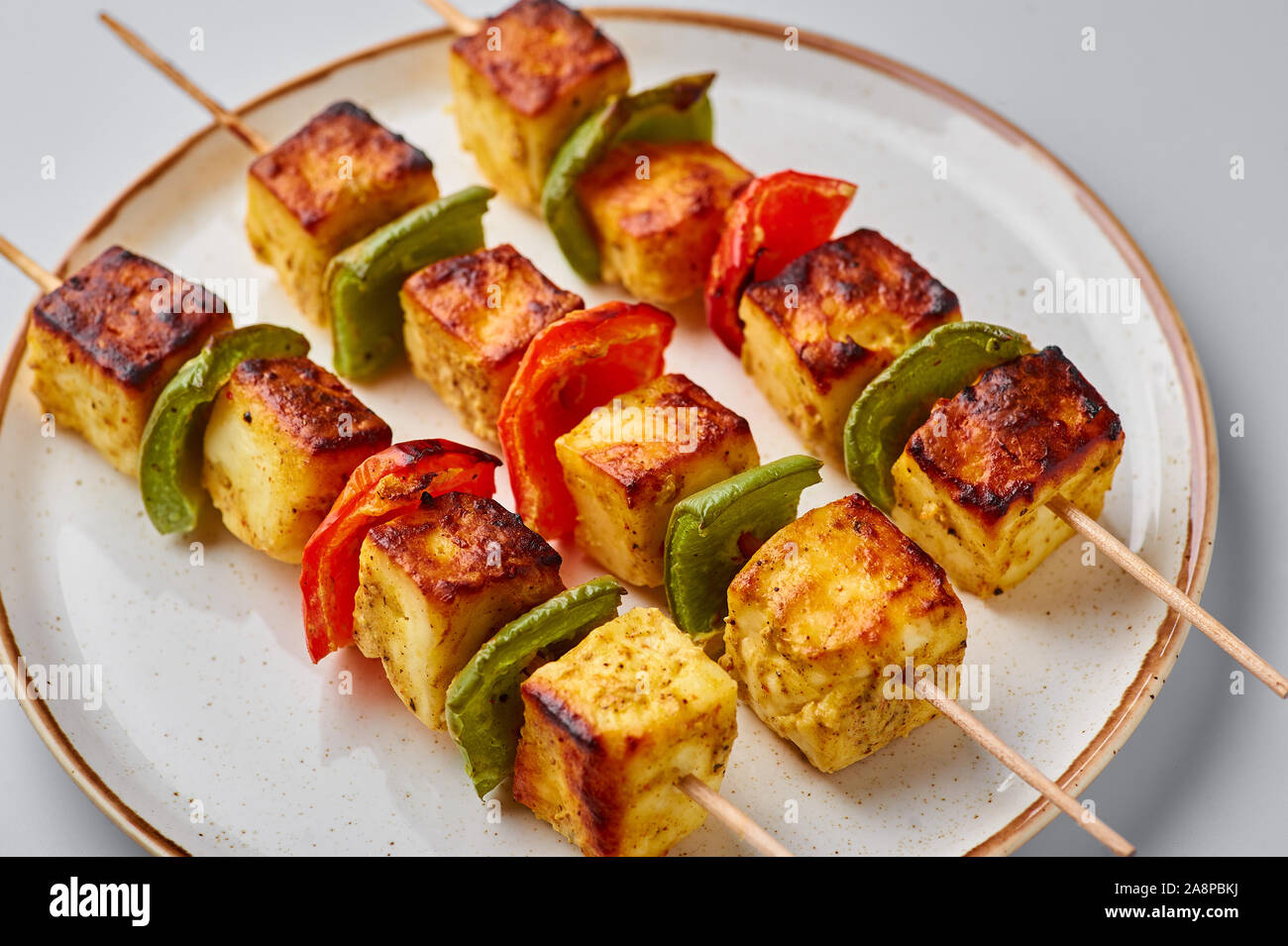 Paneer Tikka at skewers in white plate isolated at white background. Paneer tikka is an indian ...