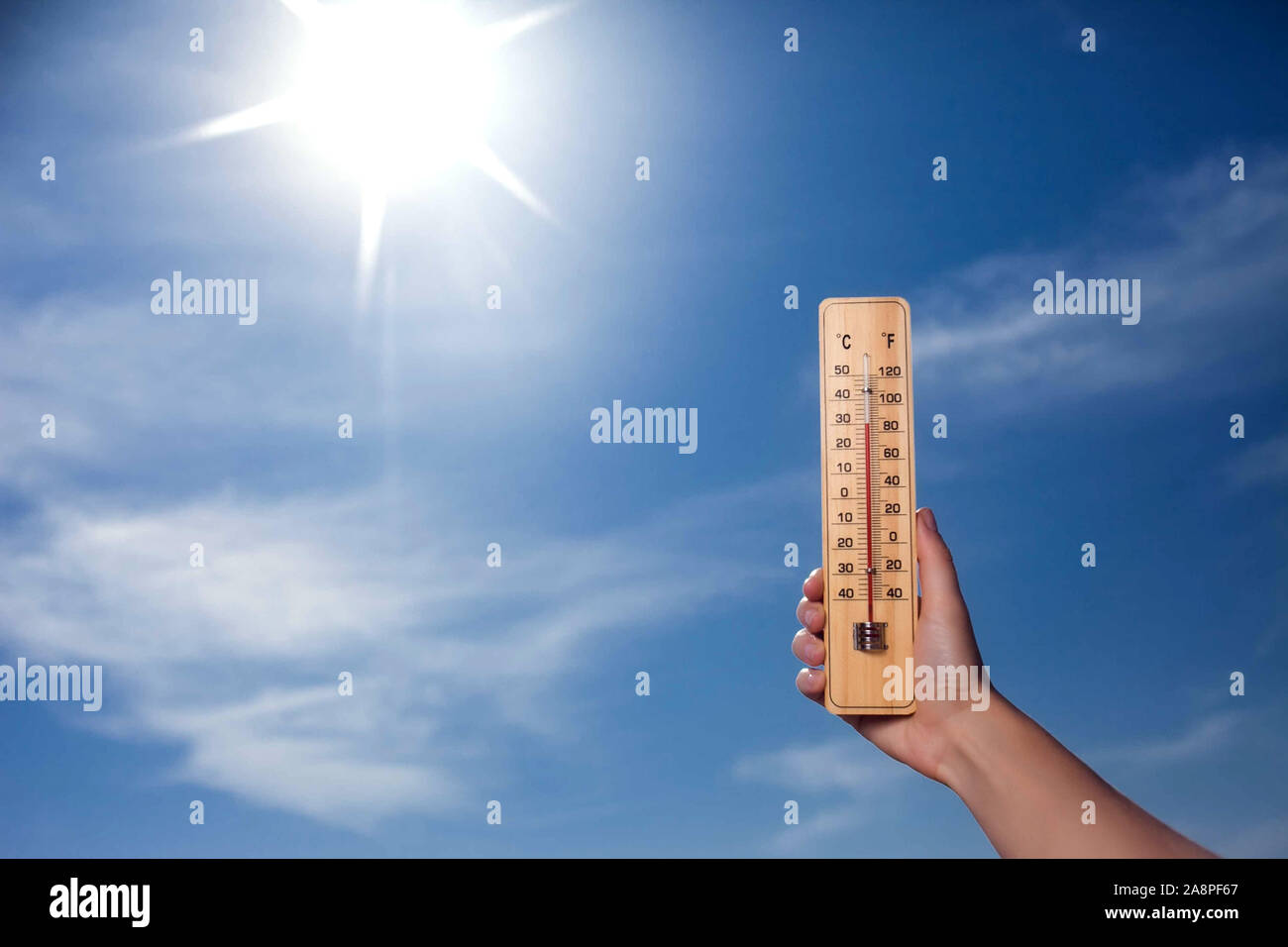 A thermometer with red scale in hand on the sky and sun background. Hot ...