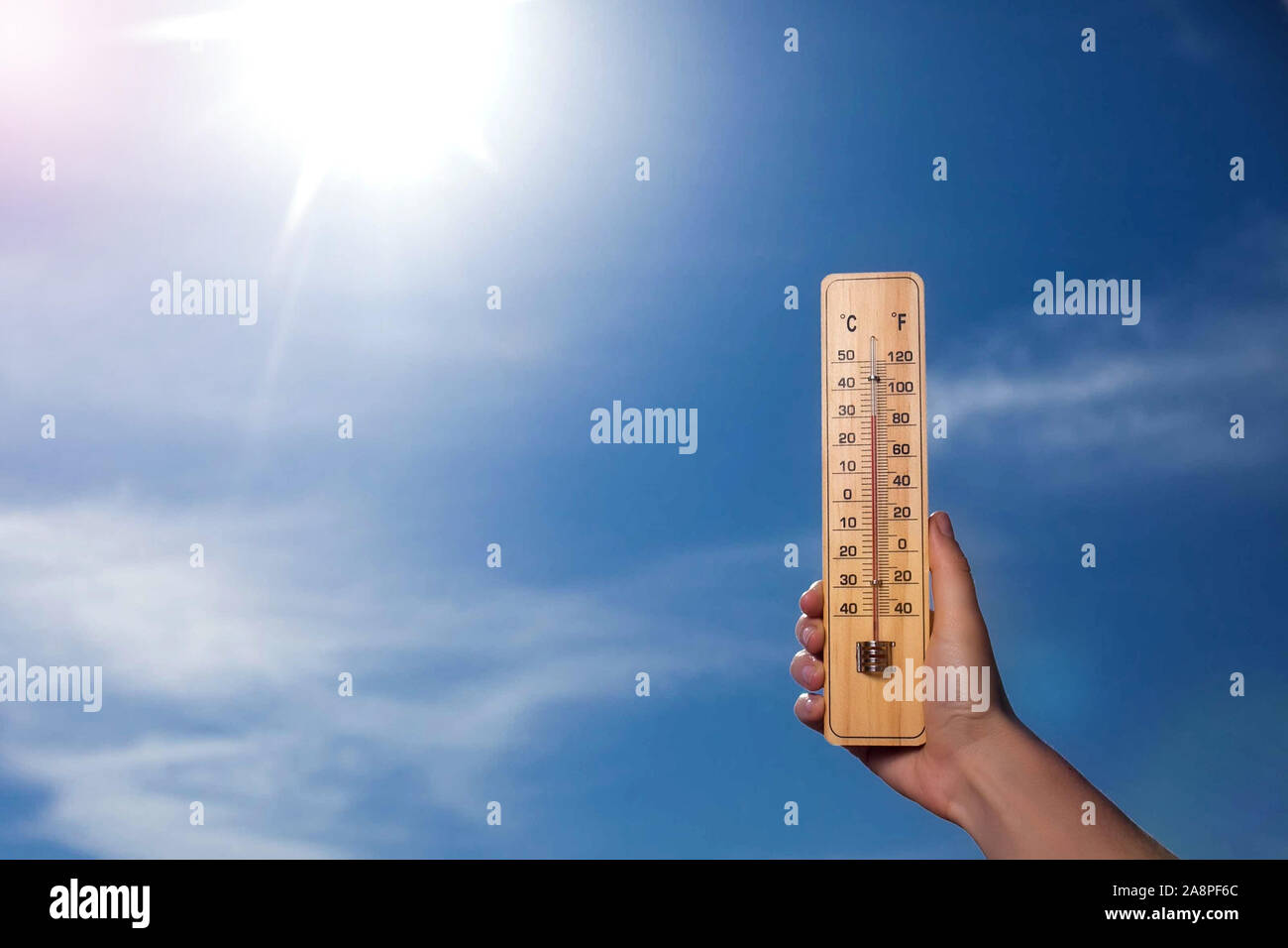 A thermometer with red scale in hand on the sky and sun background. Hot ...