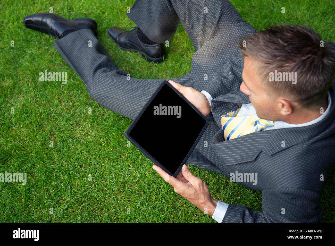 Young businessman reclining on green grass lawn using his tablet ...